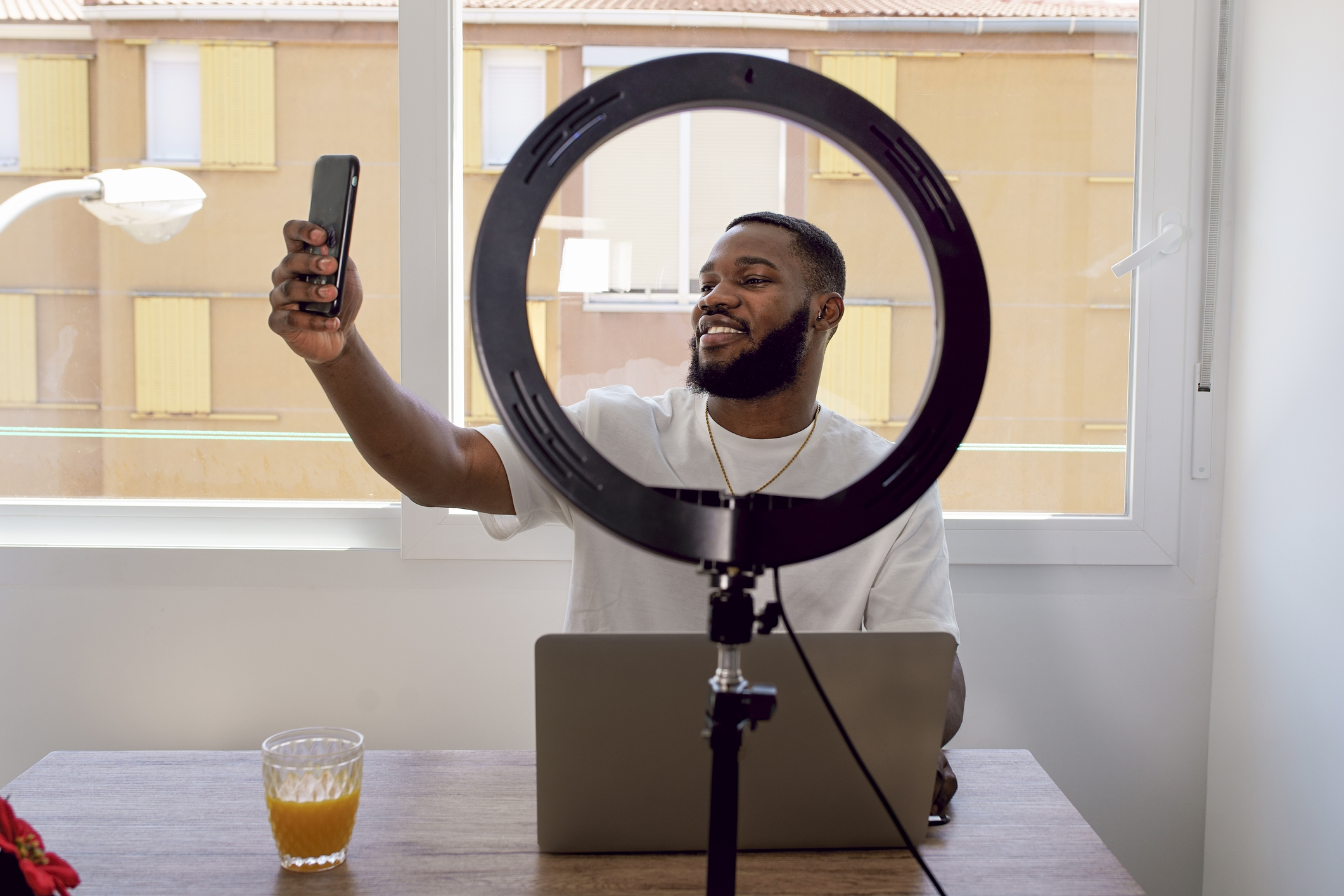 Smiling vlogger taking selfie through smart phone by laptop at home ...